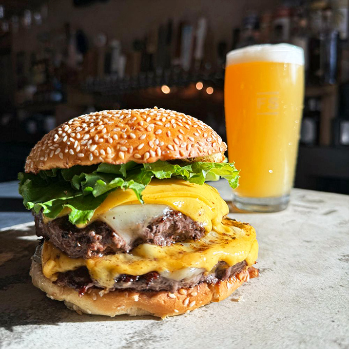 This double-decker burger with melted cheese stands proudly beside a craft beer &ndash; the dynamic duo your taste buds have been waiting for.
