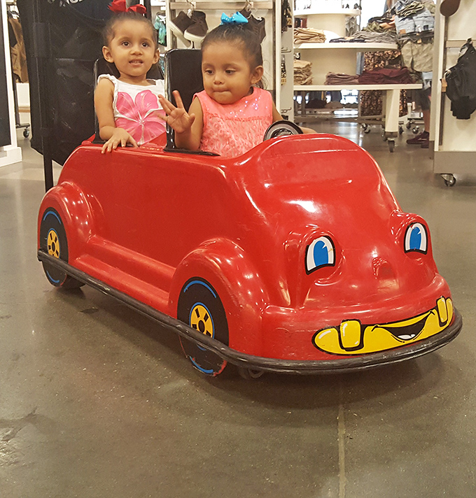 Another set of tiny shoppers-in-training enjoying a ride break. That little red car's smile matches the joy of parents who just scored half-price designer jeans. 
