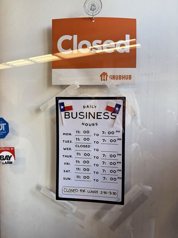 Hours posted with Texas flags standing guard. Wednesday's closure gives the smoker a day off, though our cravings never rest.