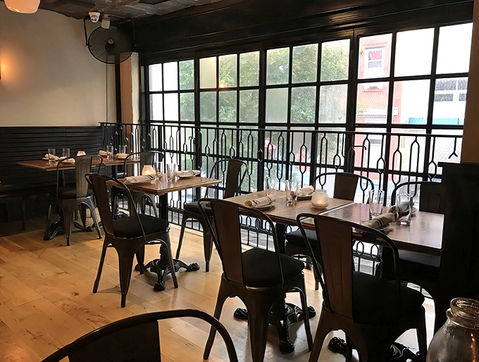 Sunlight streams through industrial windows, illuminating a dining space where conversations flow as freely as the drinks.