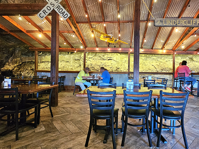 Corrugated metal ceiling, wooden beams, and that incredible rock wall create a dining space that feels both sheltered and connected to nature.