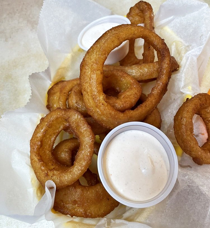 Golden onion rings stacked like delicious jewelry, with dipping sauce that makes you question why vegetables ever bothered growing any other way.