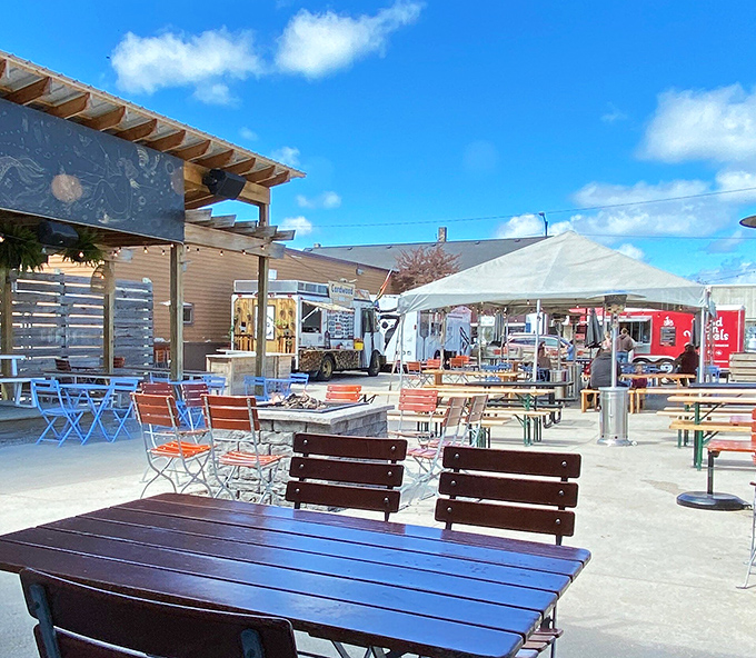 Blue skies frame the perfect Michigan afternoon—wooden tables await hungry patrons while food trucks prepare their mouthwatering offerings just steps away.