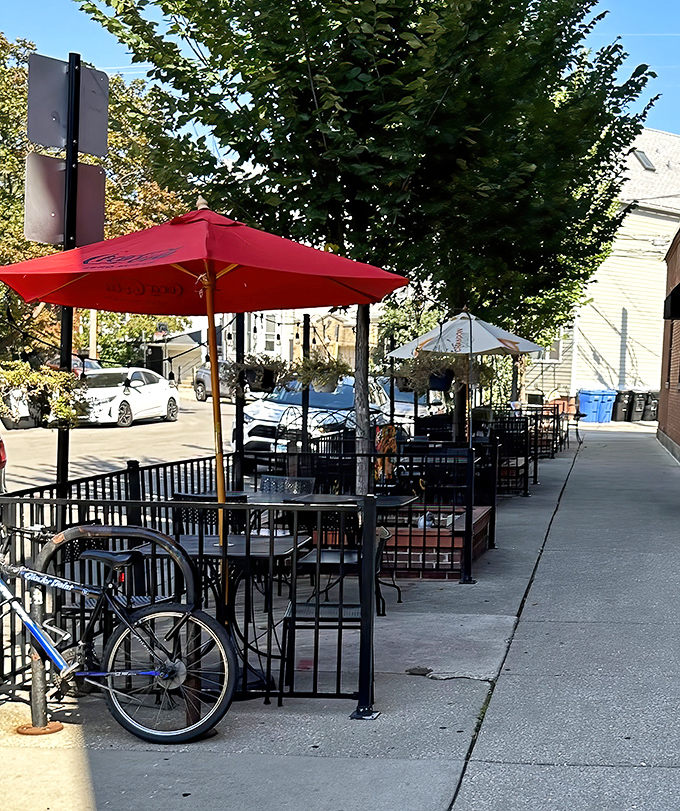 Sidewalk seating under cheerful red umbrellas, where summer evenings stretch as long as your pizza cravings.