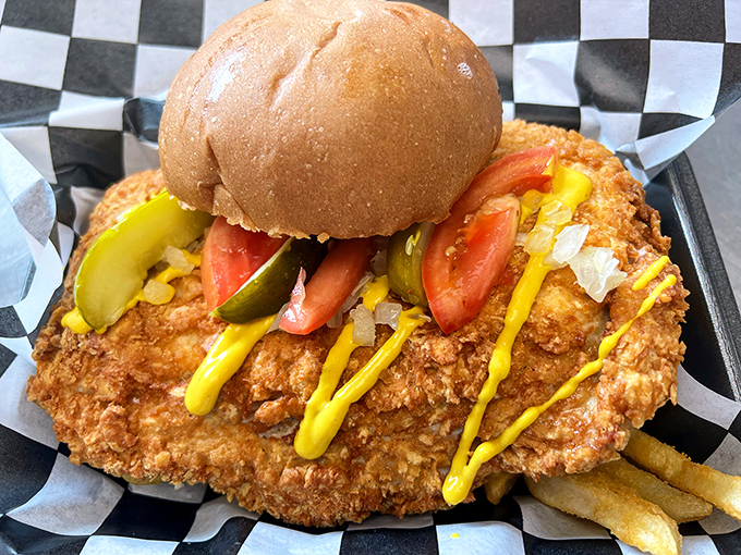 The breaded pork tenderloin &ndash; an Iowa classic that's practically hanging off the bun. Pickle, mustard, and onion complete this Midwest masterpiece.
