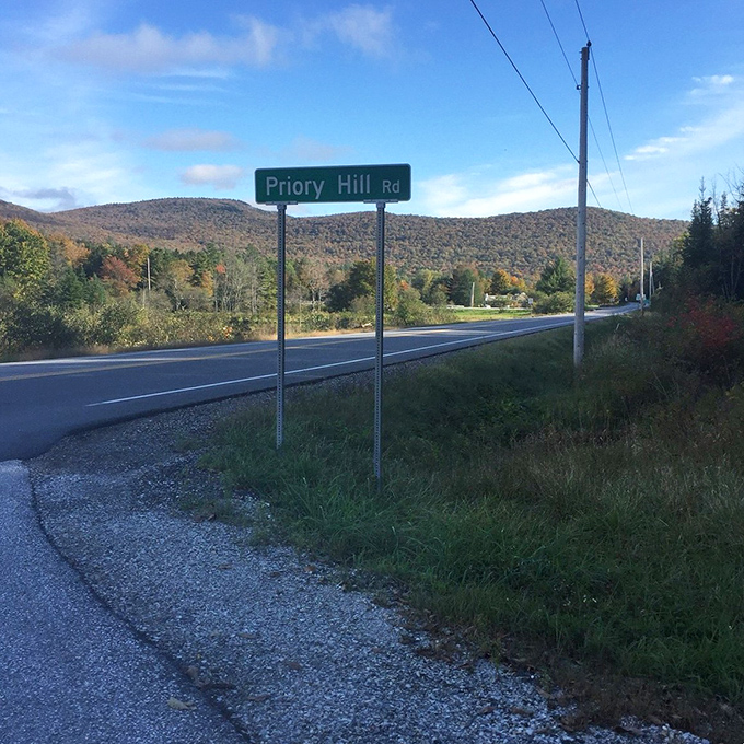 Priory Hill Road sign stands sentinel against mountains wearing their autumn best &ndash; a humble marker pointing toward extraordinary beauty.
