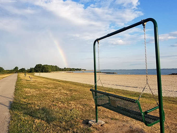 Rainbow arcs over beach swing, proving Mother Nature understands perfect Instagram staging better than any influencer ever could.