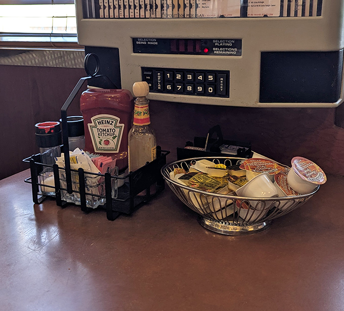 Condiment station that's the unsung hero of diner culture &ndash; ketchup, sweeteners, and creamers standing at attention like tiny soldiers ready for breakfast battle.