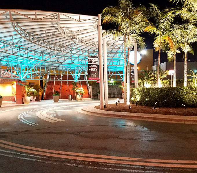 The mall's exterior at night transforms into a glowing retail spaceship, ready to beam shoppers up to discount heaven. Those palm trees add tropical drama.