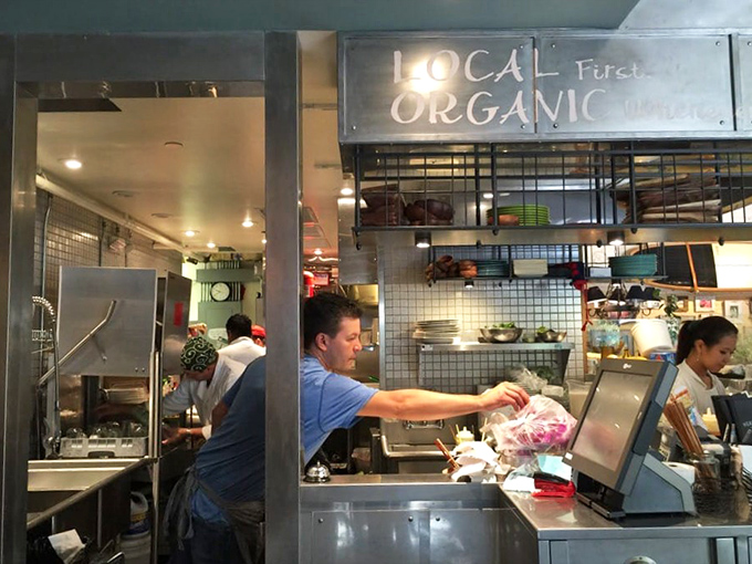 The kitchen proudly announces "LOCAL ORGANIC" above busy hands transforming island ingredients into memories you'll try to recreate at home.