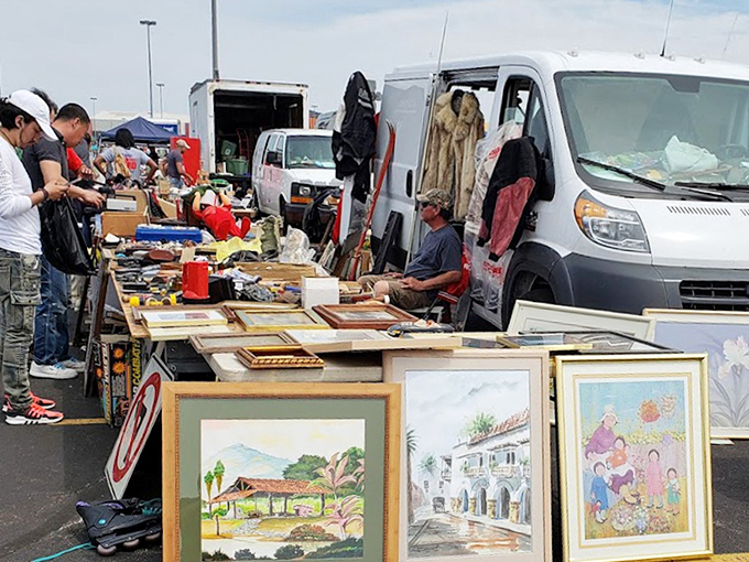 Framed artwork leans hopefully against a vendor's van. Someone painted these desert scenes and family portraits with dreams of Sotheby's, not parking lots.