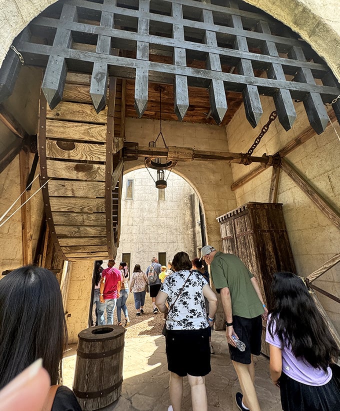 Visitors explore beneath the imposing portcullis, experiencing authentic medieval castle entrance architecture and defensive features.
