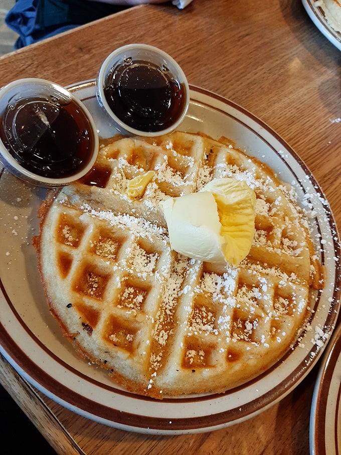 A Belgian waffle that's dressed for success with powdered sugar, butter, and syrup standing by. Breakfast or dessert? Yes.