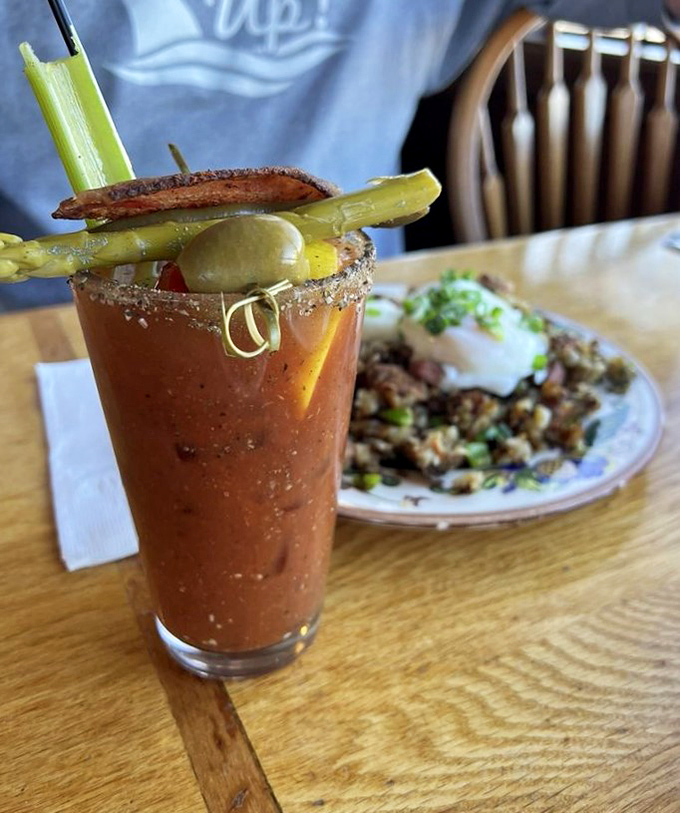 A Bloody Mary that's practically a meal, standing tall beside what appears to be a hearty hash &ndash; weekend brunch perfection in liquid and solid form.