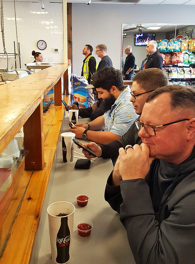 The universal language of anticipation: hungry patrons at the counter, phones down, minds focused on the imminent arrival of sandwich bliss.