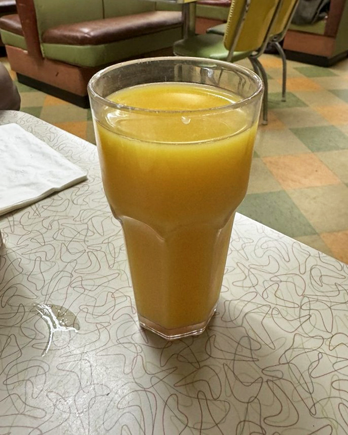 Orange juice so vibrant it could power a small city. Vitamin C never looked so appealing against that classic checkerboard floor.