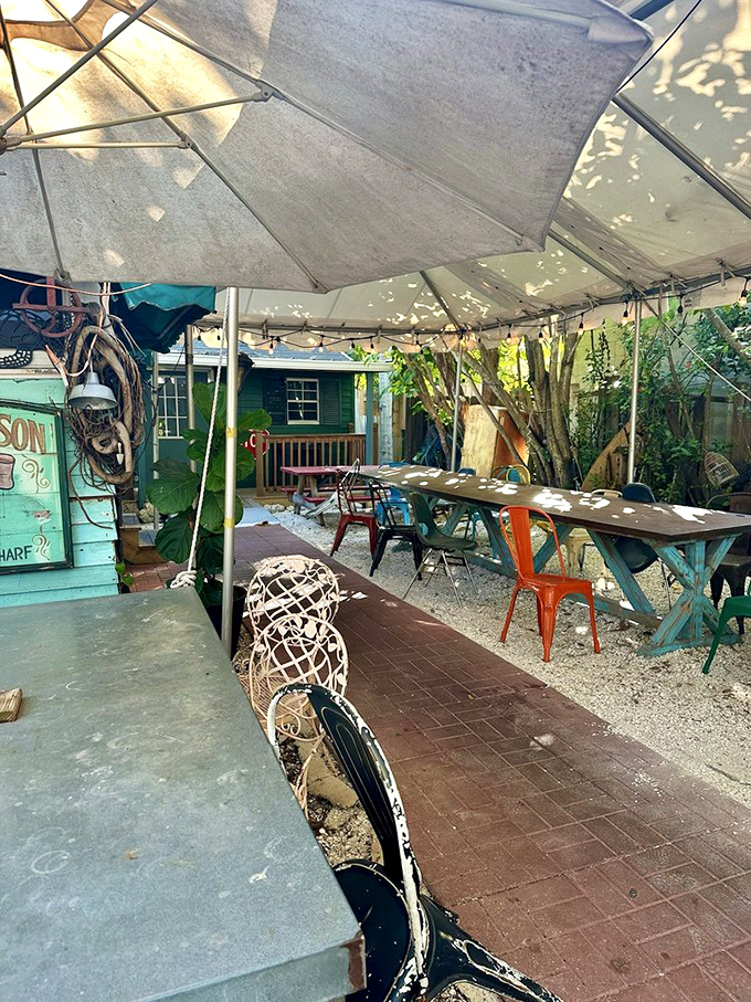 The outdoor seating area offers a whimsical escape with mismatched furniture and dappled sunlight filtering through canvas&mdash;like dining in a Wes Anderson film set in Florida.