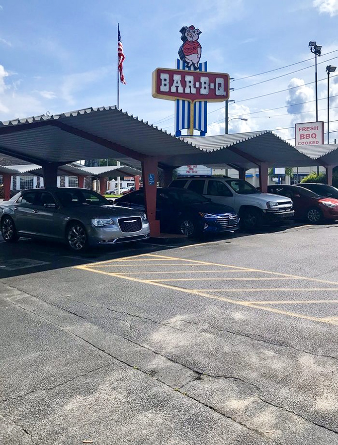 The covered parking area beneath that iconic pig sign &ndash; where cars gather like hungry pilgrims at a barbecue shrine.