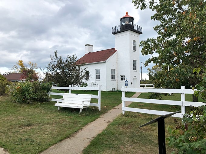 Sand Point Lighthouse stands pristine against the landscape, its whitewashed walls and rustic bench inviting visitors to pause and contemplate maritime history.
