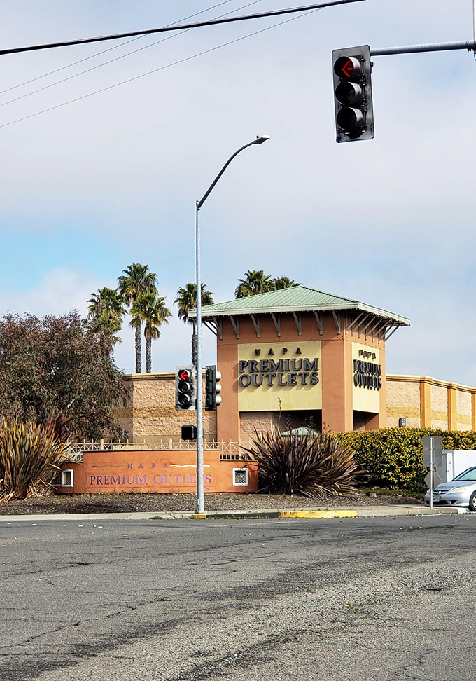 The entrance sign stands tall like a retail lighthouse, guiding bargain-hunters safely to shore. Those red traffic lights mean "stop spending" (said no one ever).