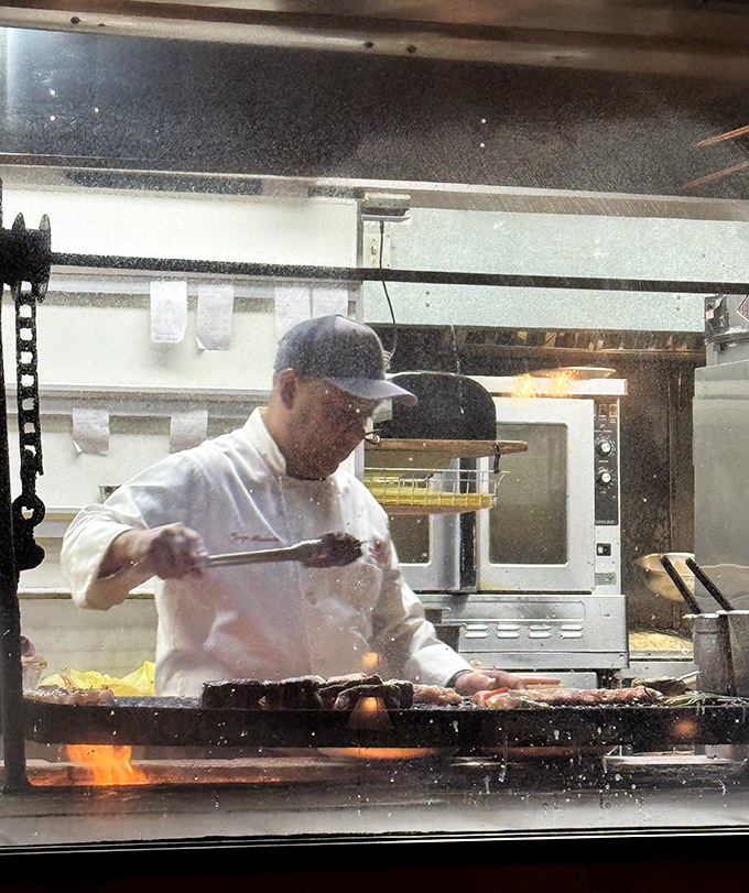 Behind the glass, culinary magic happens as oak fire transforms raw ingredients into the stuff of road trip legends.