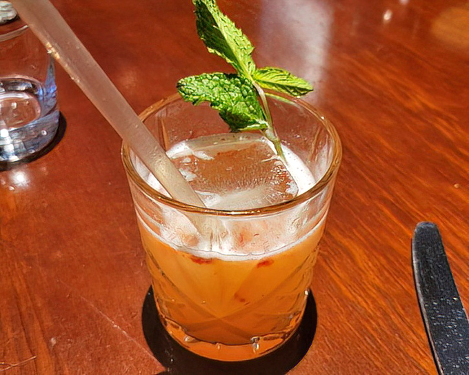The cocktail arrives with a sprig of mint standing at attention, like a tiny soldier guarding the treasure of flavors waiting below the ice.