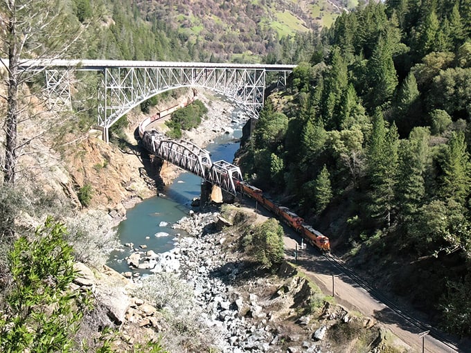A freight train snakes alongside the river, dwarfed by the canyon's grandeur. Even massive engines look like toys in nature's playground.