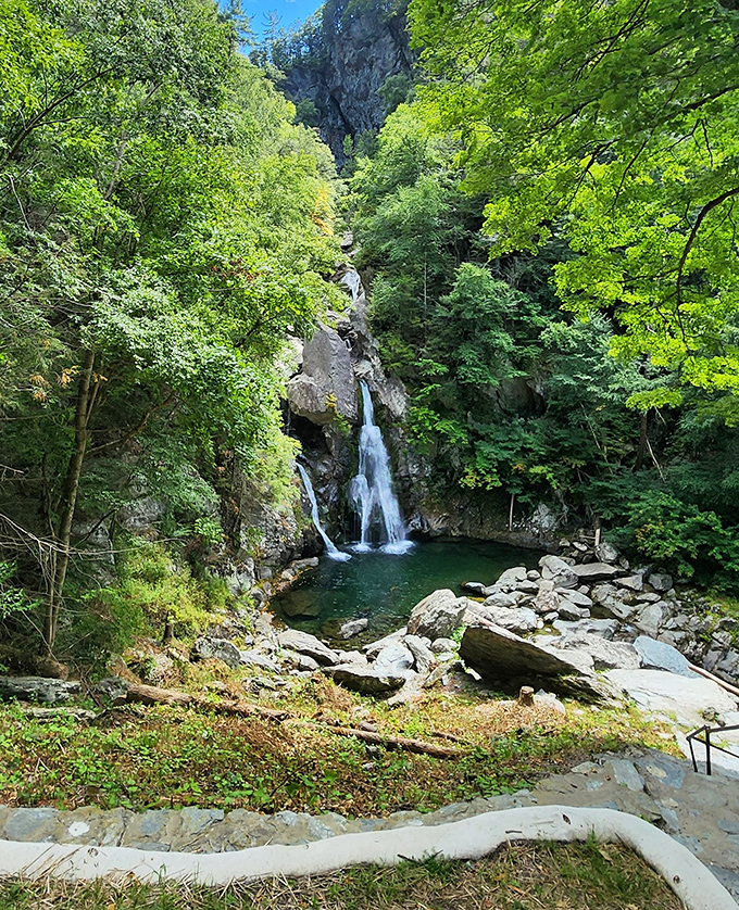 The approach reveals Bash Bish Falls framed by verdant summer foliage, creating a natural theater for water's dramatic plunge into the emerald pool below.