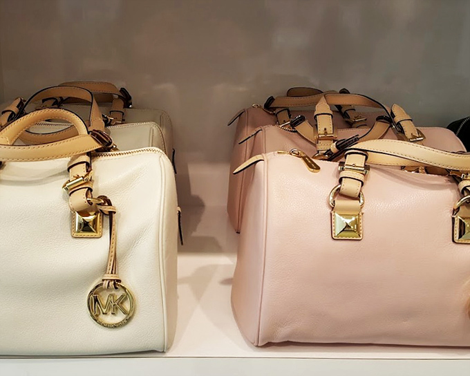 Michael Kors handbags stand at attention like soldiers of style. Their leather gleams under display lights, practically begging for a new home.