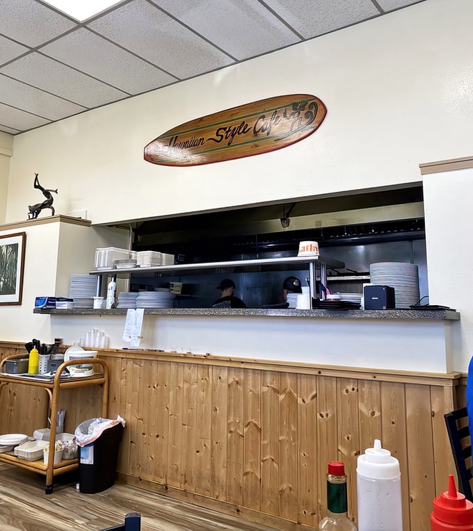 The pass where kitchen magic becomes plate reality. That surfboard watches over everything like a guardian of flavor.