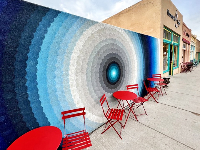 The hypnotic blue mural outside creates a vortex that pulls you toward those cherry-red tables. Sidewalk seating that's practically performance art. 