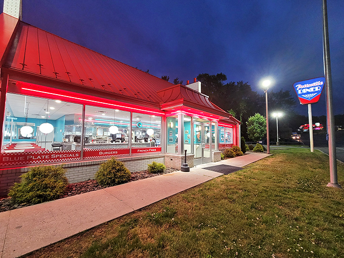 As night falls, the diner glows like a ruby against the darkening sky, a neon promise of American classics done right.