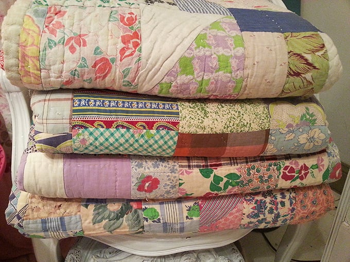 Handmade quilts stacked like chapters of American crafting history. Each stitch tells a story your guest bedroom is dying to share.