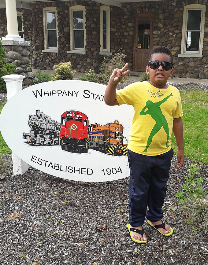 A young enthusiast points excitedly at the Whippany Station sign. His expression captures the pure joy that trains still inspire in visitors of all ages.