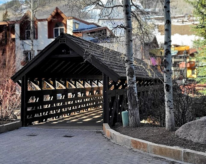 In winter's bare-branch season, the bridge's dark timber frame stands in stark contrast to Vail's colorful village buildings peeking through in the background.