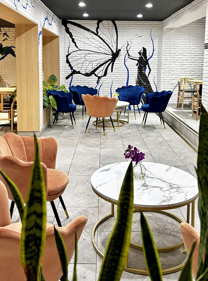 The butterfly mural watching over coral and navy velvet chairs creates a space that's Instagram-worthy without trying too hard.