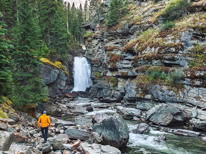 A solitary explorer in bright orange provides scale to the falls, reminding us that sometimes we're just small players in nature's grand theater.