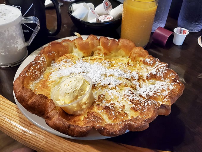 The German pancake rises from its plate like a golden souffle cloud, dusted with powdered sugar snow and waiting for its butter glacier to melt.