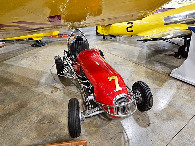 A classic midget racer nestled beneath aircraft wings &ndash; proof that speed demons come in all sizes. This little red number probably corners better than anything above it.