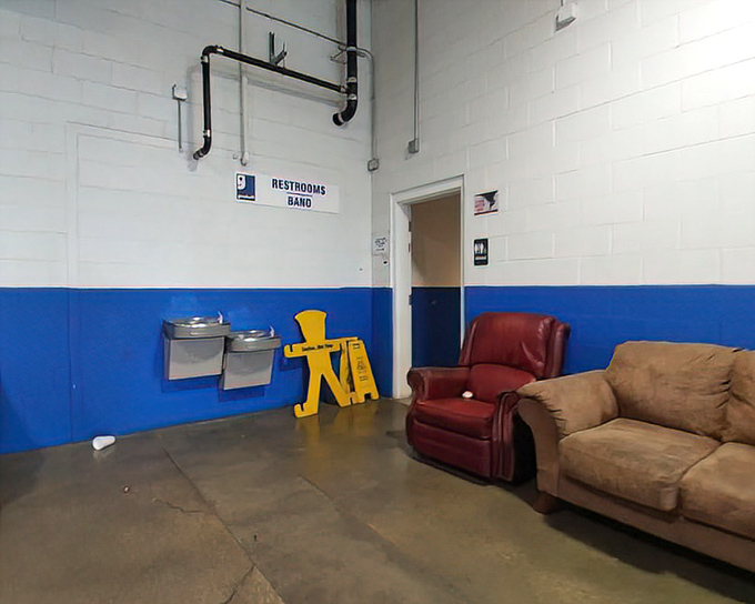Cozy chairs sit beside the restroom entrance at the Goodwill Outlet, creating a quirky little rest spot near fountains and bright signs.