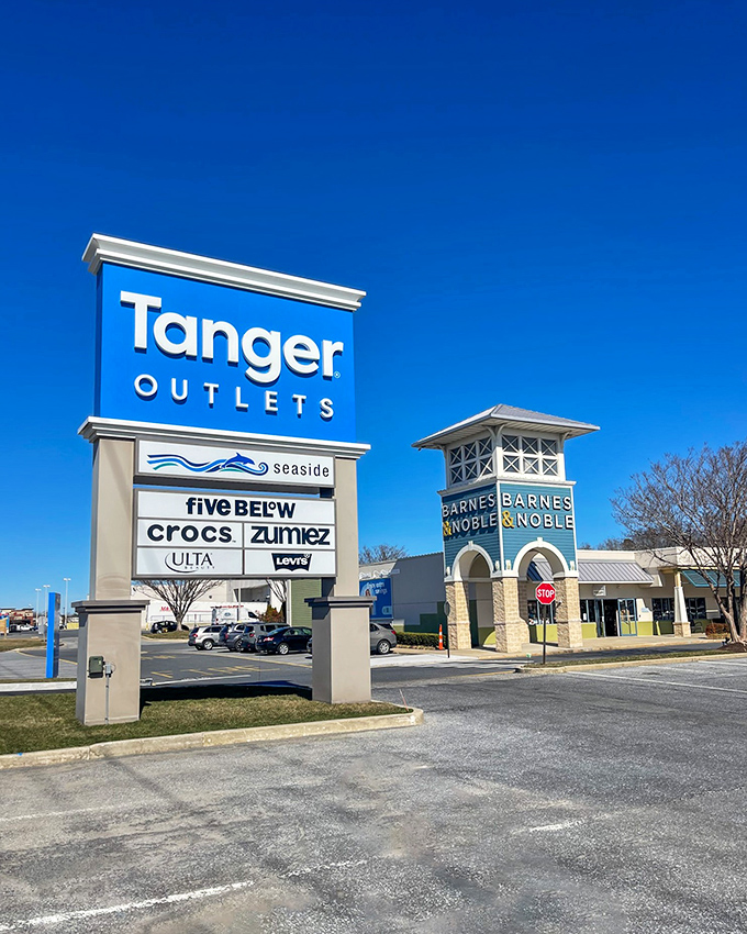The iconic Tanger sign stands against a perfect blue sky, a beacon calling to shoppers with the siren song of "designer brands at outlet prices."