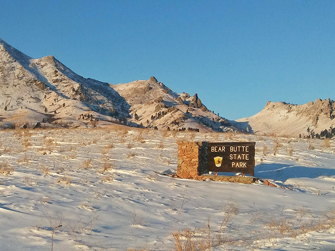 Winter transforms Bear Butte into a snow-dusted wonderland, where the park sign stands as a promise of natural beauty in every season.