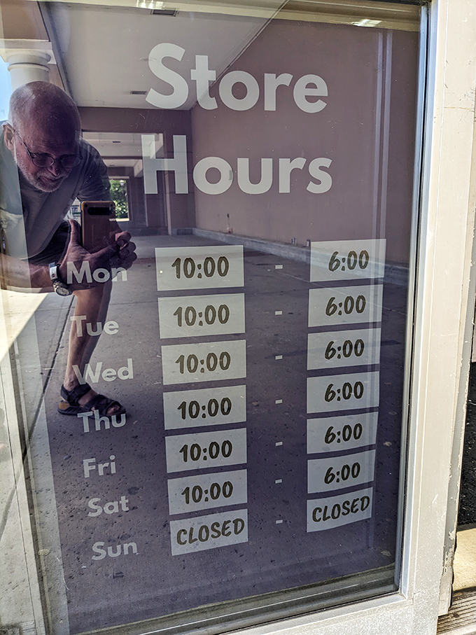 Store hours posted clearly—open six days a week for your bargain-hunting pleasure. The reflection captures a shopper already documenting their finds for posterity.