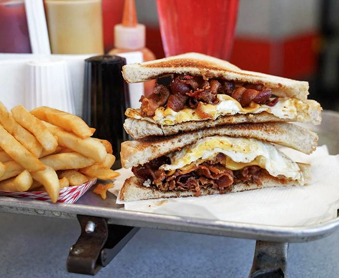 The breakfast sandwich—where crispy bacon and eggs unite between toast in a morning masterpiece that makes alarm clocks almost worth the rude awakening.