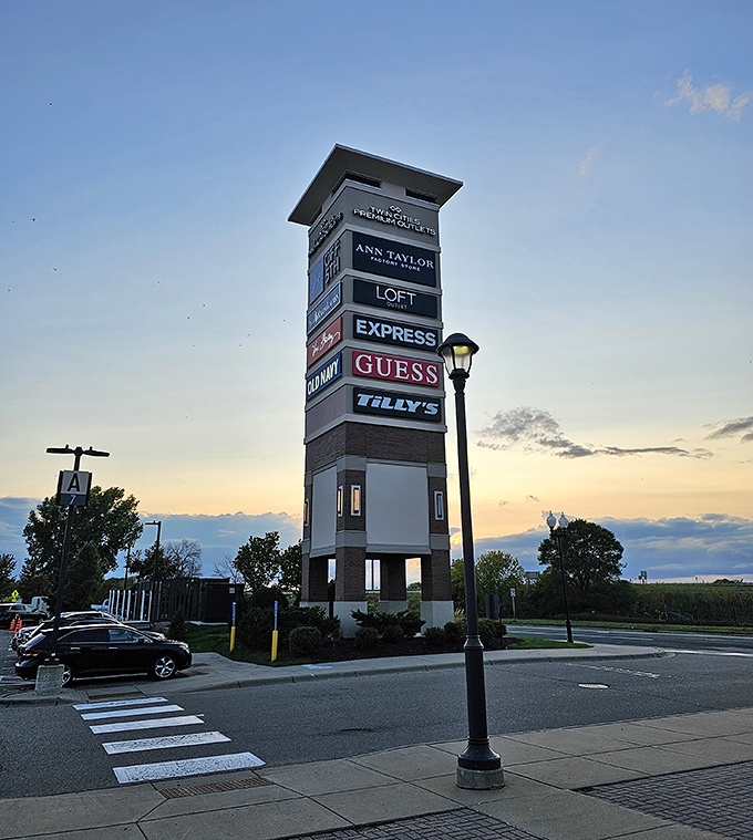 The outlet mall's towering sign stands like a retail lighthouse, guiding bargain hunters safely to shore as the sun sets on another day of discount adventures.