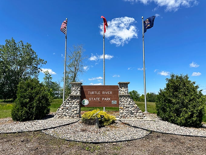 The park entrance sign stands proudly beneath three flags, a stone gateway to your next great outdoor adventure.