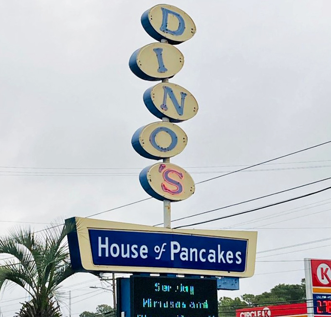 The vertical DINOS sign stands tall against the sky, a retro beacon calling hungry travelers like a pancake lighthouse on the breakfast shore.