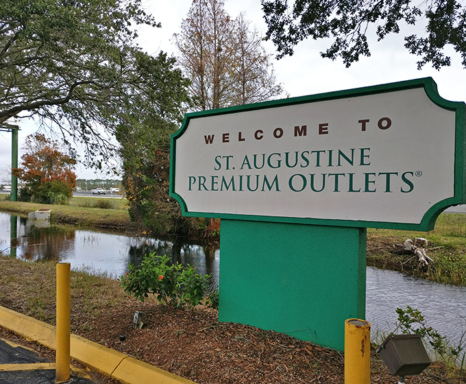 The welcoming sign nestled among Florida greenery—your first hint that wallet-friendly retail therapy lies just beyond.