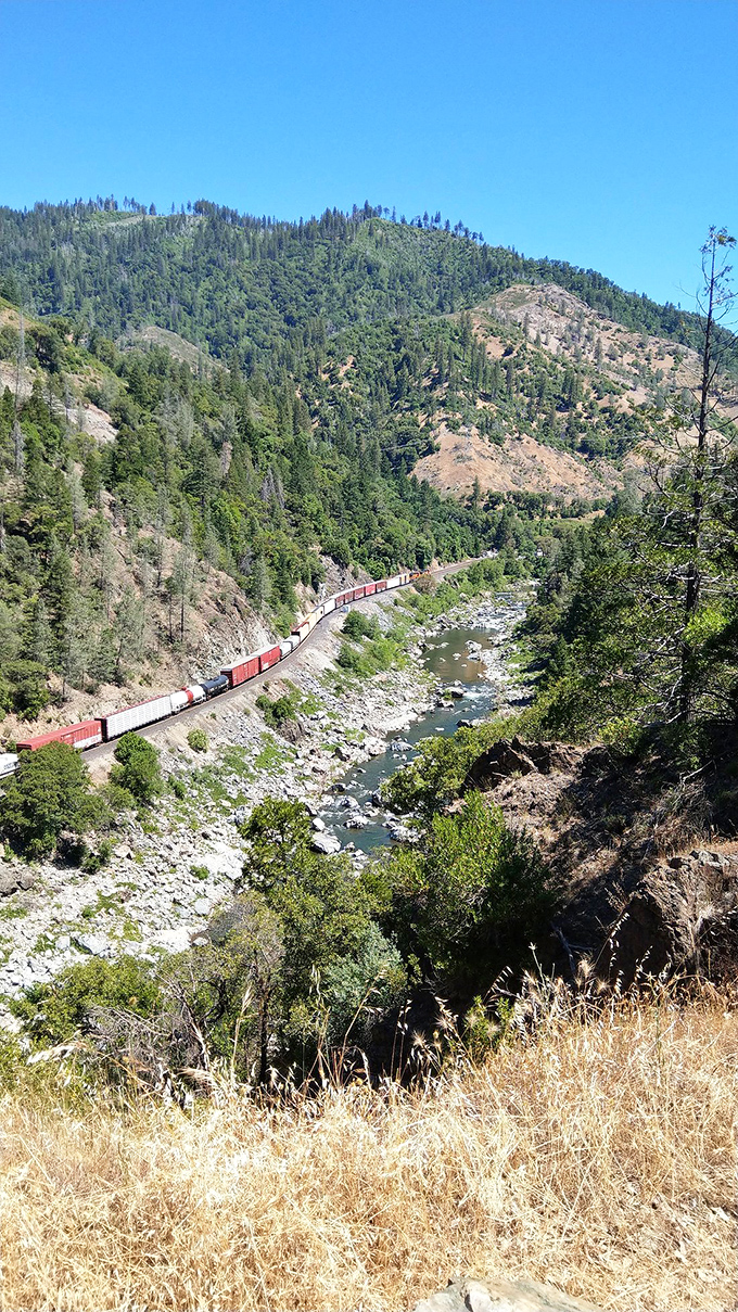 Sun-drenched hillsides frame the canyon where train tracks and river have coexisted for generations. A California classic that never goes out of style.