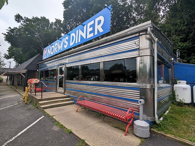 Norm's Diner gleams in classic blue and silver, like a time machine disguised as a lunch counter. The red bench outside invites weary travelers to rest before diving into breakfast bliss.